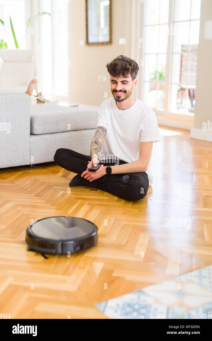 Young man using automatic vacuum cleaner to clean the floor, controling ...