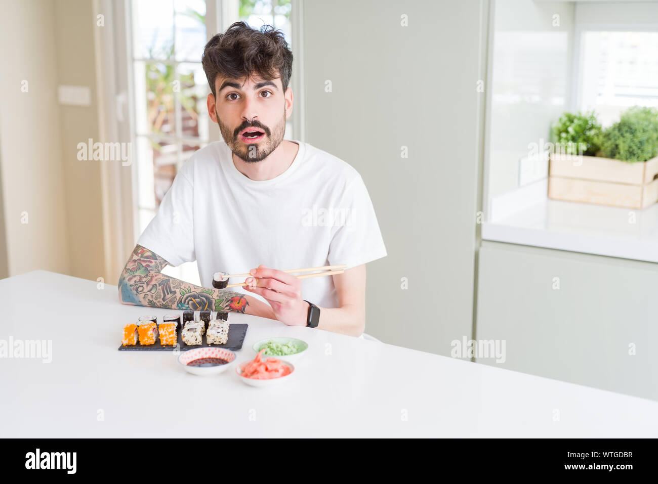 Young man eating asian sushi from home delivery scared in shock with a ...