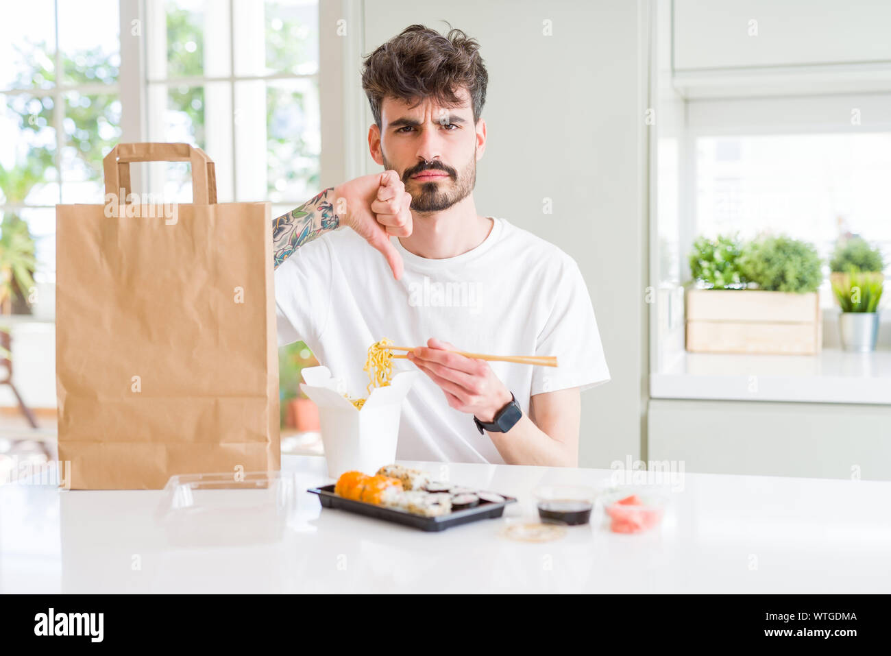 Young man eating asian sushi from home delivery with angry face ...