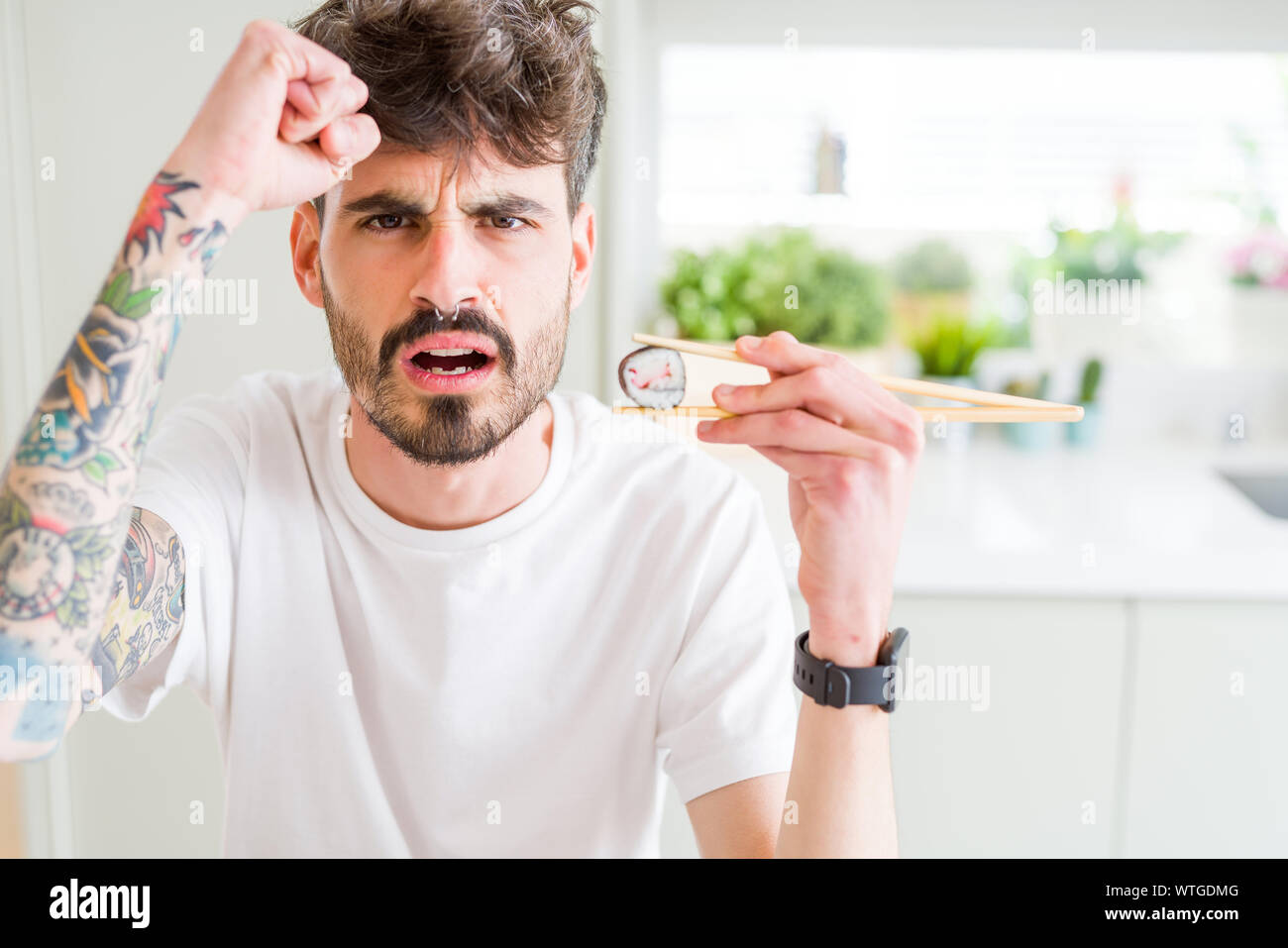 Young man eating asian sushi using chopsticks annoyed and frustrated ...