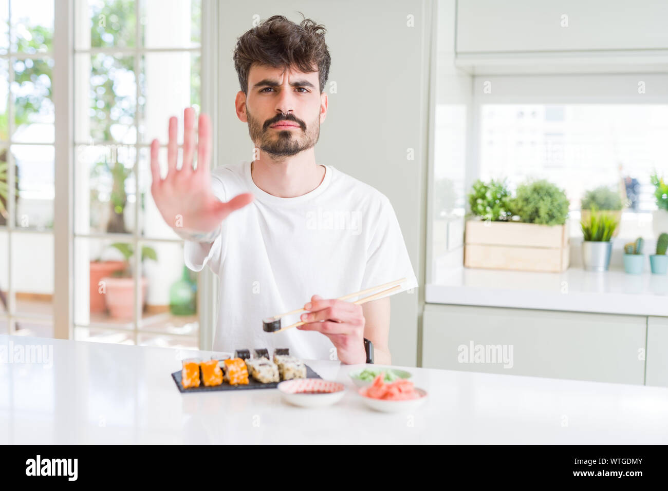 Young man eating asian sushi from home delivery with open hand doing ...