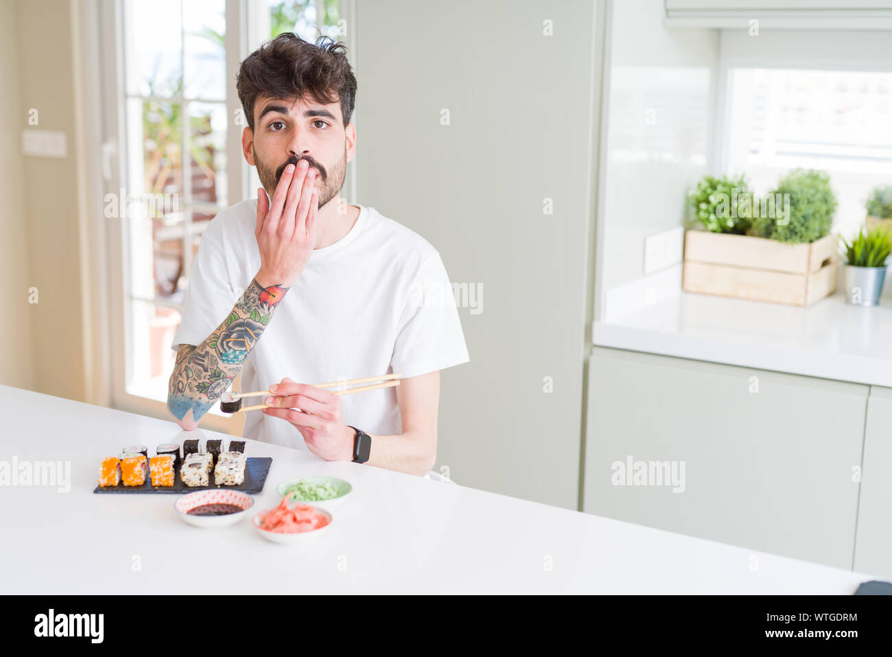 Young man eating asian sushi from home delivery cover mouth with hand ...