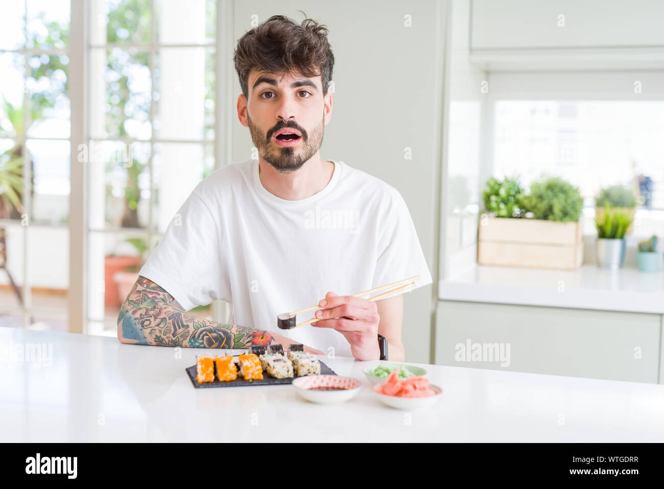 Young man eating asian sushi from home delivery scared in shock with a ...