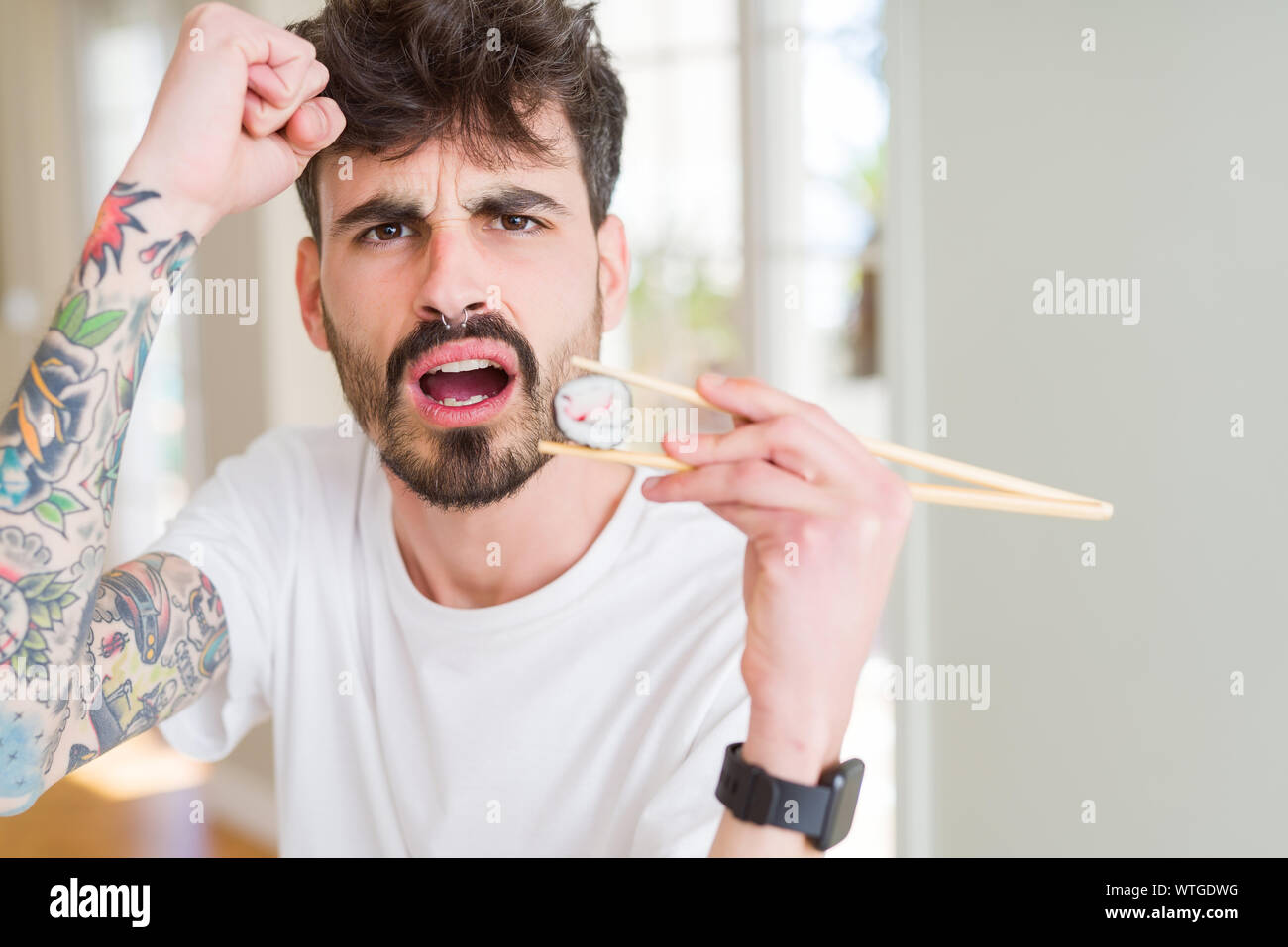 Young man eating asian sushi using chopsticks annoyed and frustrated ...