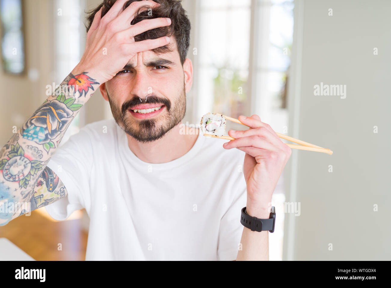 Young man eating asian sushi using chopsticks stressed with hand on ...