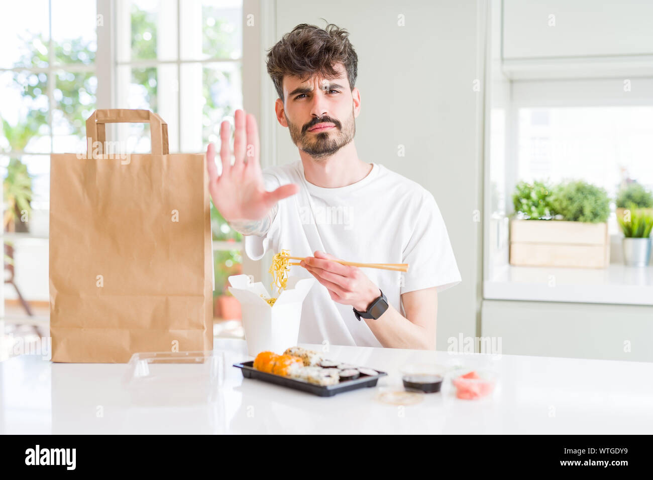 Young man eating asian sushi from home delivery with open hand doing ...