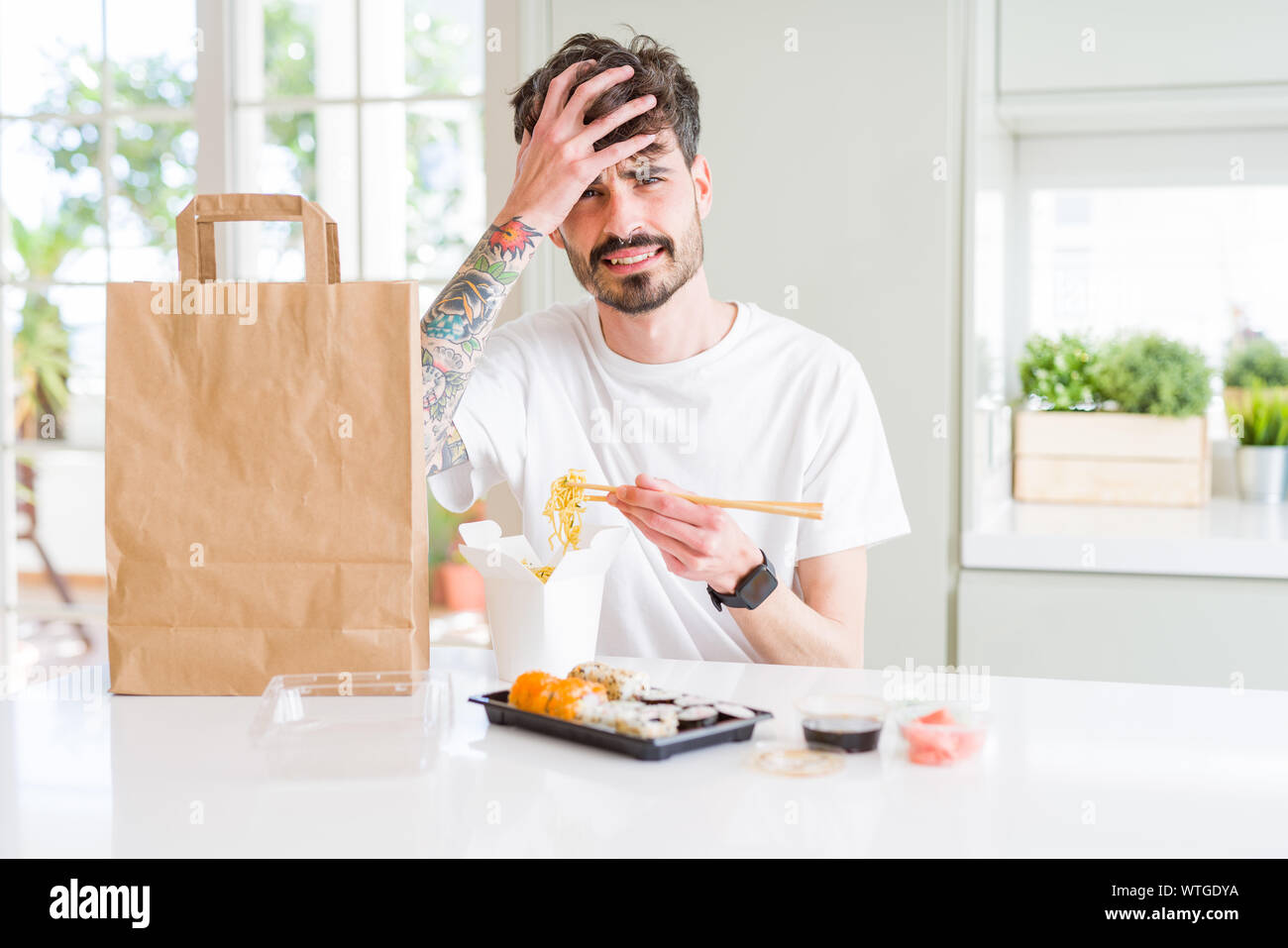 Young man eating asian sushi from home delivery stressed with hand on ...