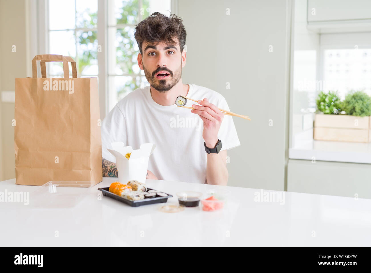 Young man eating asian sushi from home delivery scared in shock with a ...