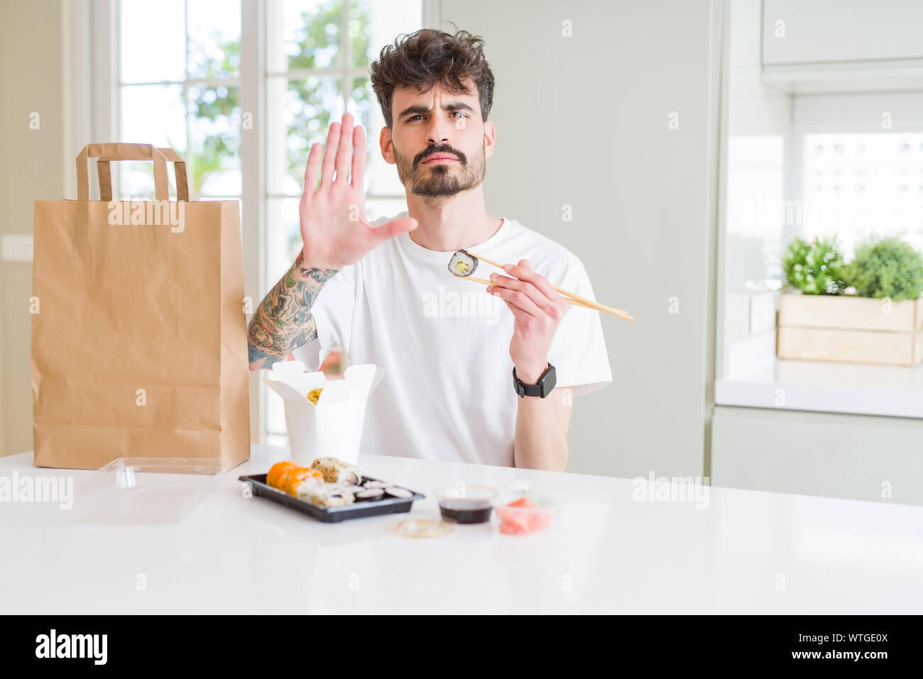Young man eating asian sushi from home delivery with open hand doing ...