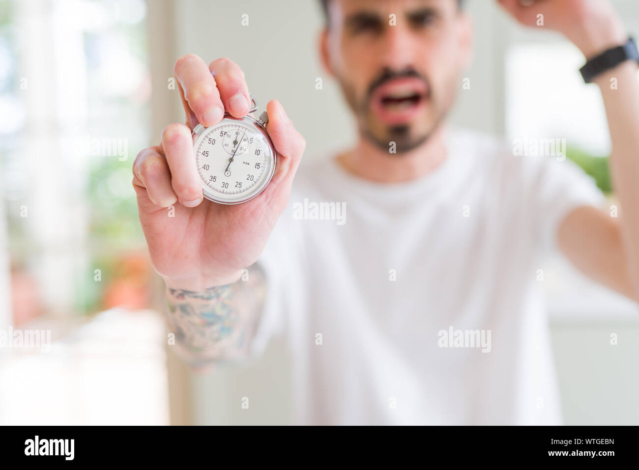 Young man using holding stopwatch annoyed and frustrated shouting with ...
