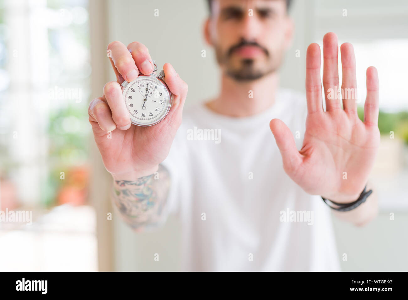 Young man using holding stopwatch with open hand doing stop sign with ...
