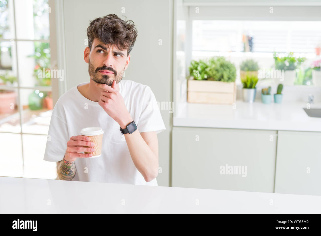 Young man drinking a coffee in a paper cup in the morning serious face ...