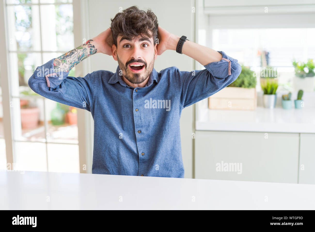 Young man wearing casual shirt sitting on white table Crazy and scared ...