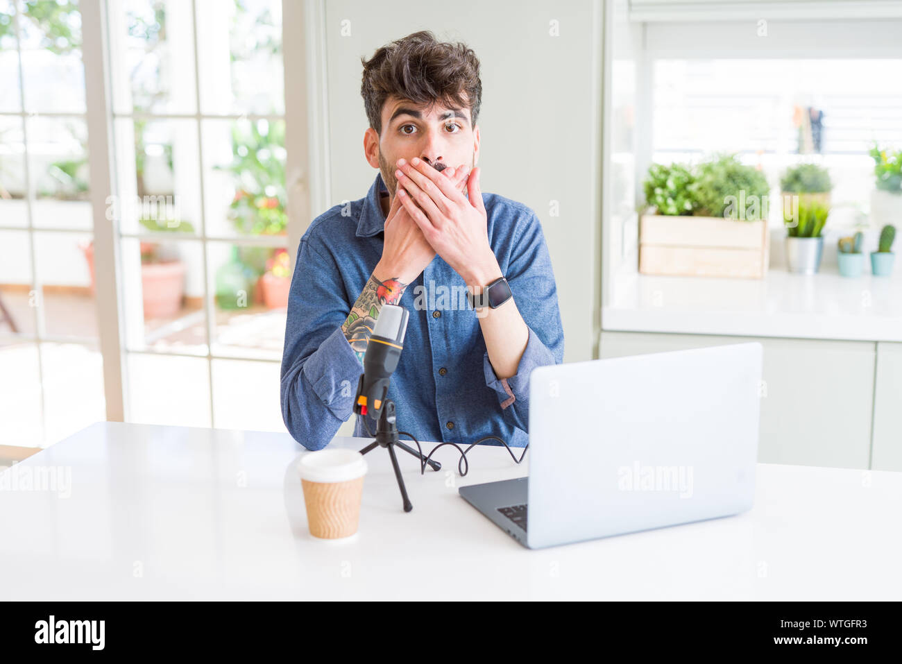 Young man recording podcast using microphone and laptop shocked ...