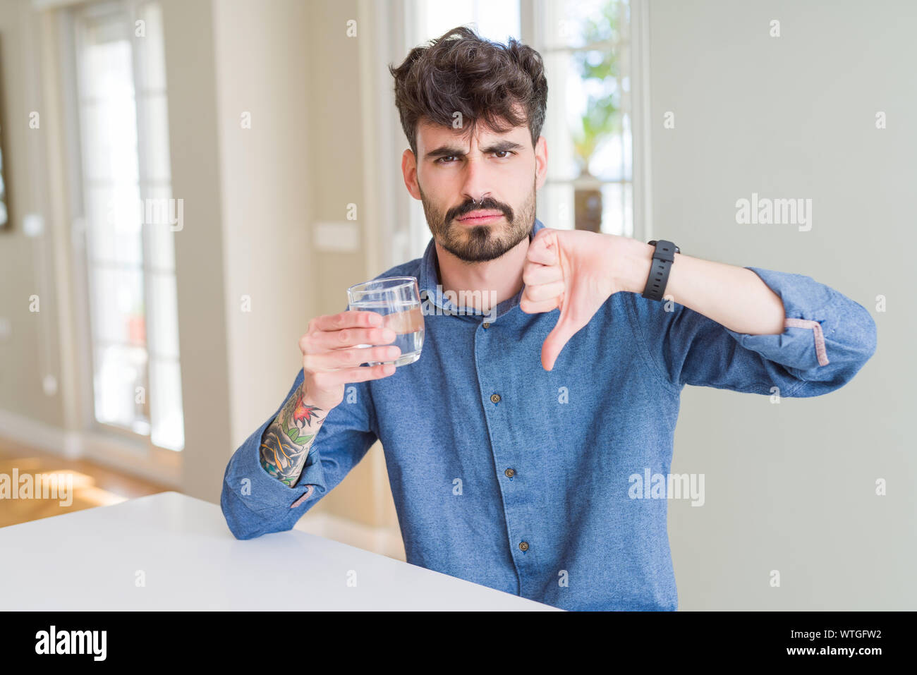 Young man drinking a fresh glass of water with angry face, negative ...