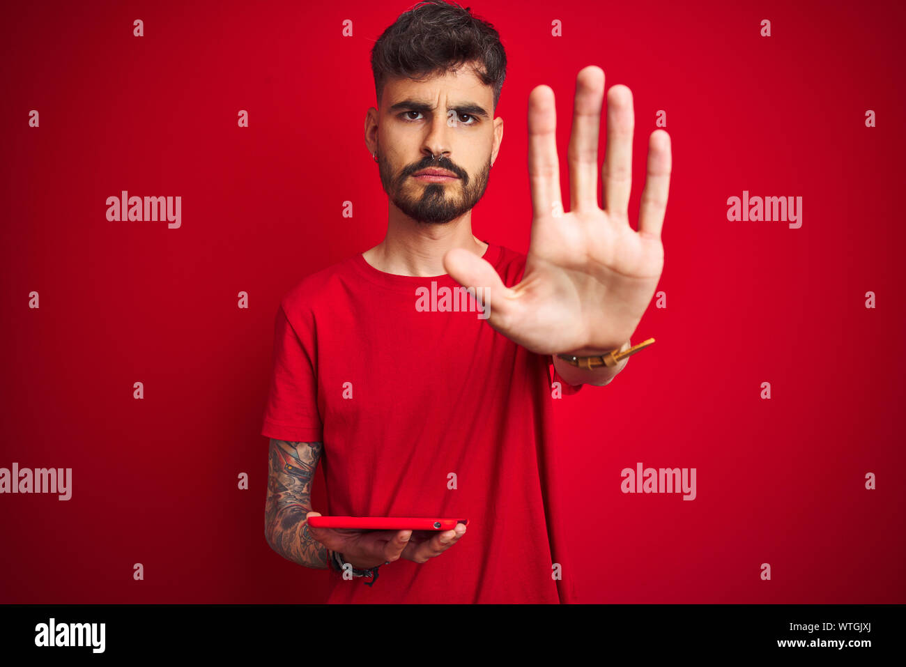 Young man with tattoo using tablet standing over isolated red ...