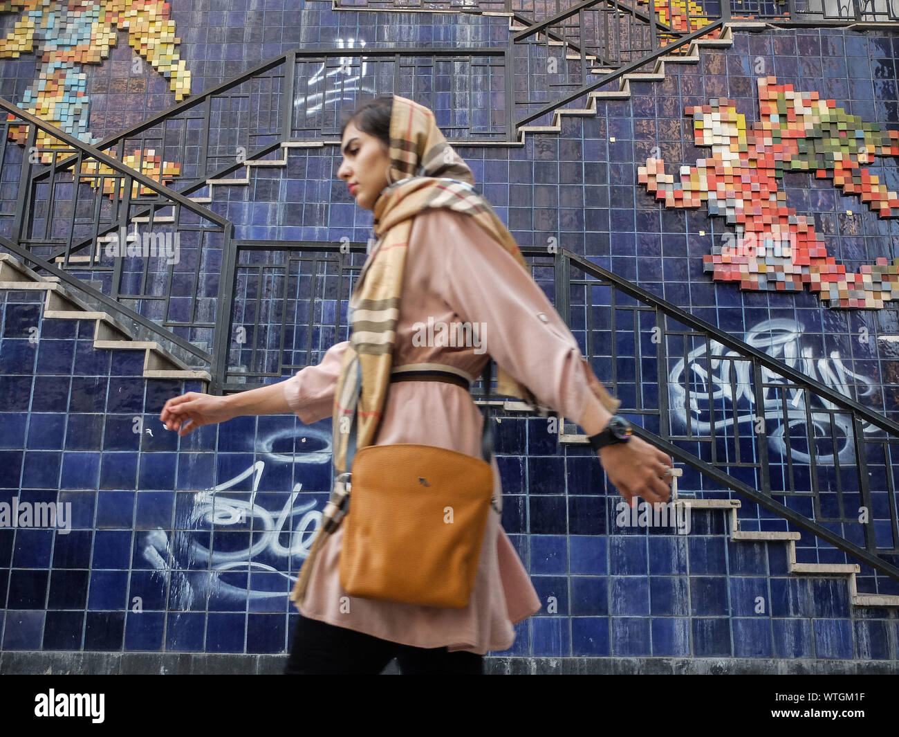Tehran, Iran. 12th Sep, 2019. A woman walks past a mural in a sidewalk ...