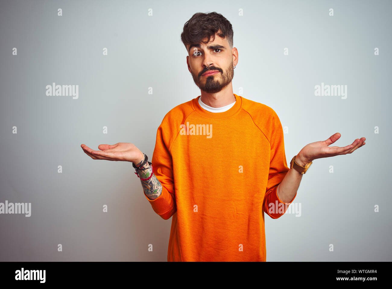 Young man with tattoo wearing orange sweater standing over isolated ...