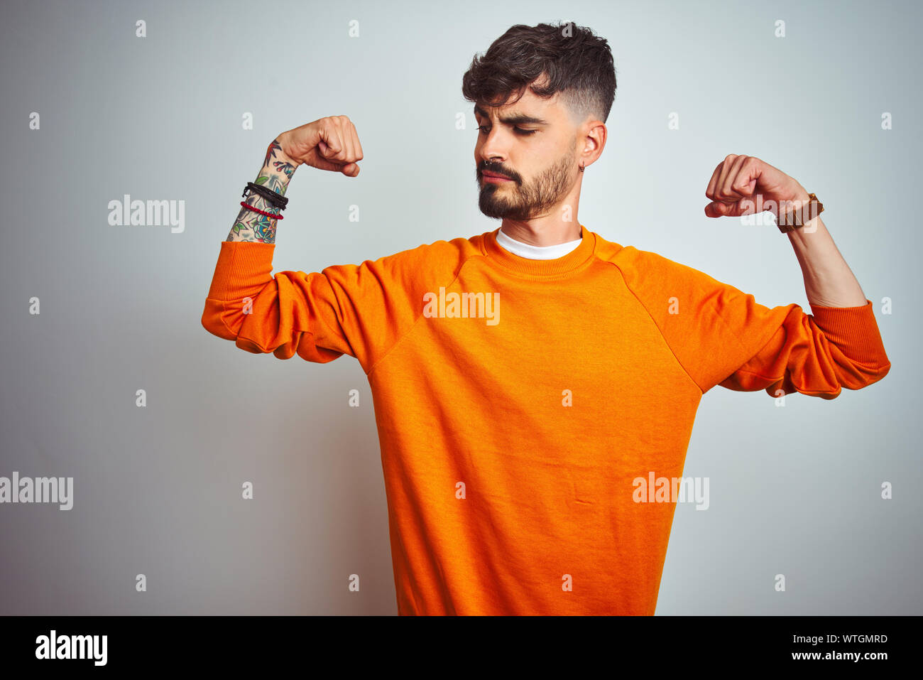 Young man with tattoo wearing orange sweater standing over isolated ...