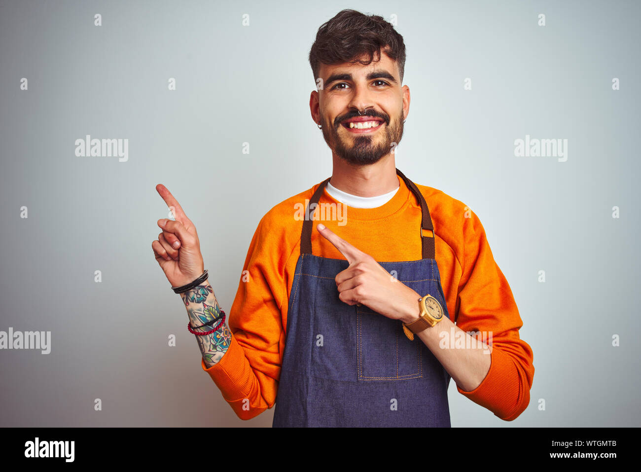 Young shopkeeper man with tattoo wearing apron standing over isolated ...