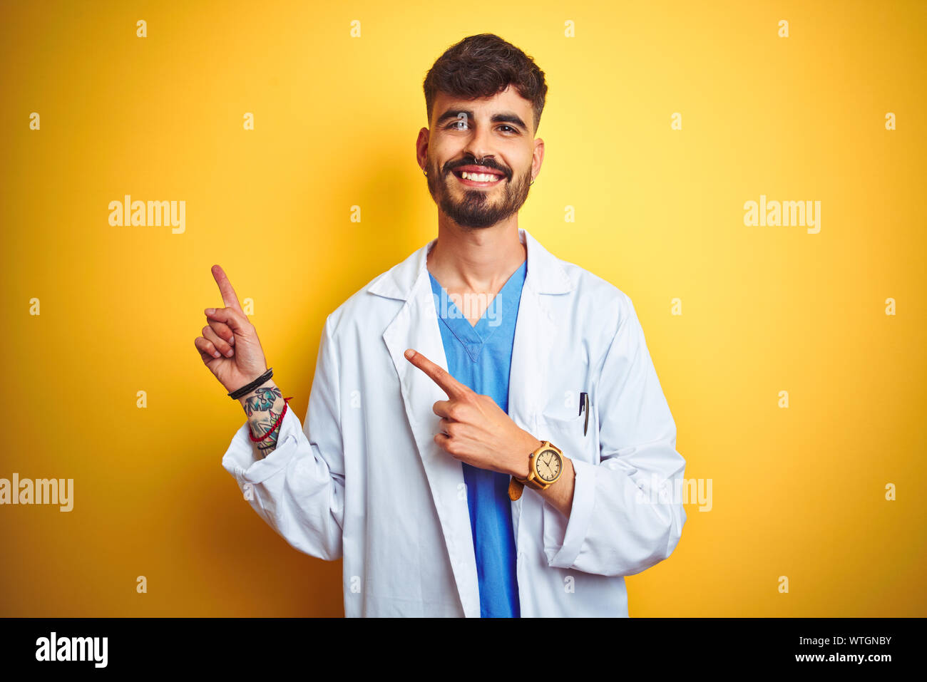 Young doctor man with tattoo standing over isolated yellow background ...