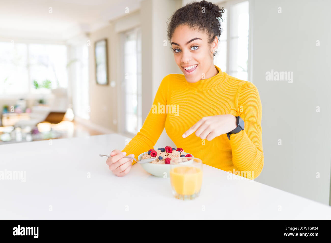 Young african american girl eating healthy cereals for breakfast very happy pointing with hand ...