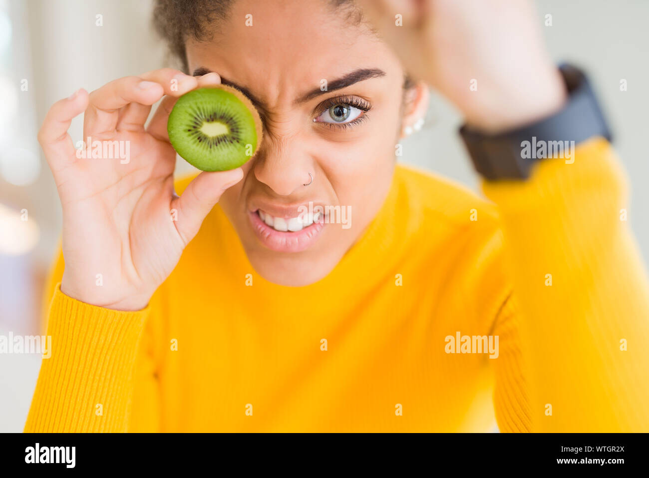 Young african american girl eating green kiwi annoyed and frustrated ...
