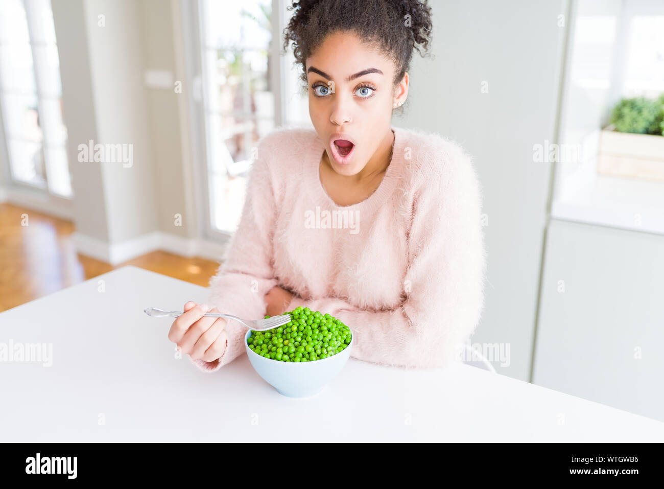 Young african american girl eating healthy green peas scared in shock ...