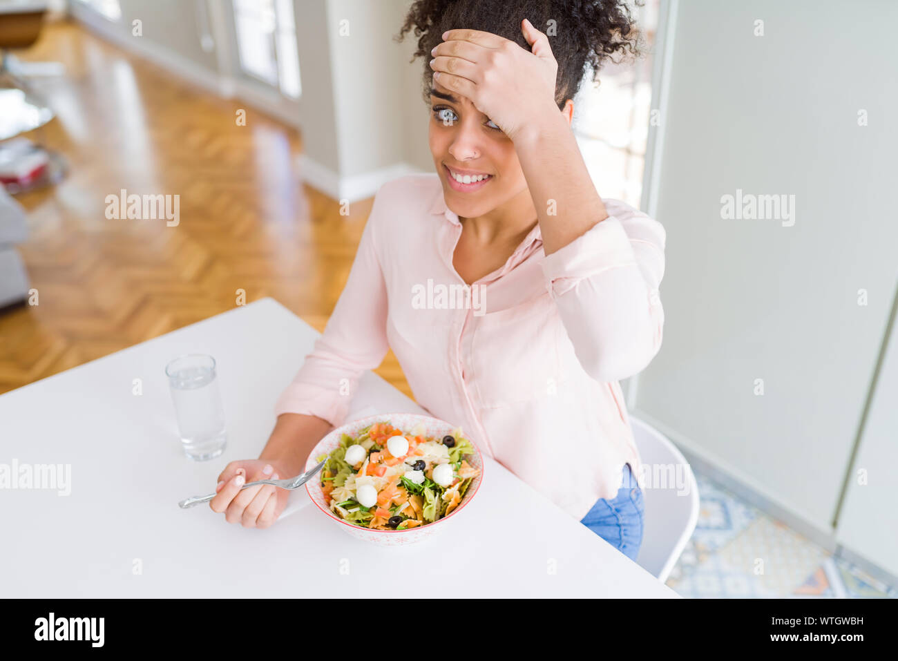 Young african american woman eating healthy pasta salad stressed with ...