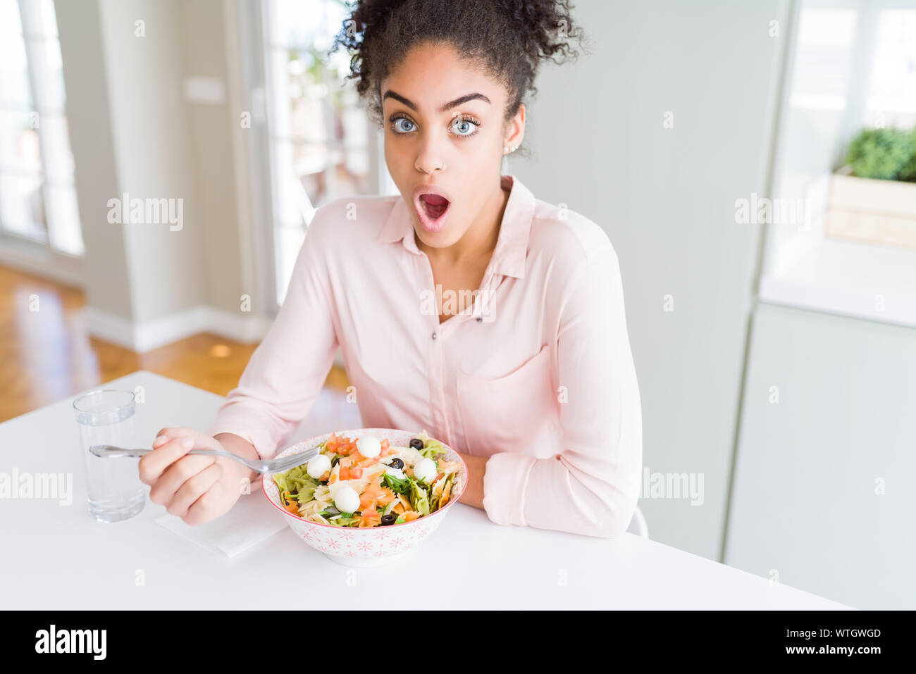 Young african american woman eating healthy pasta salad scared in shock ...