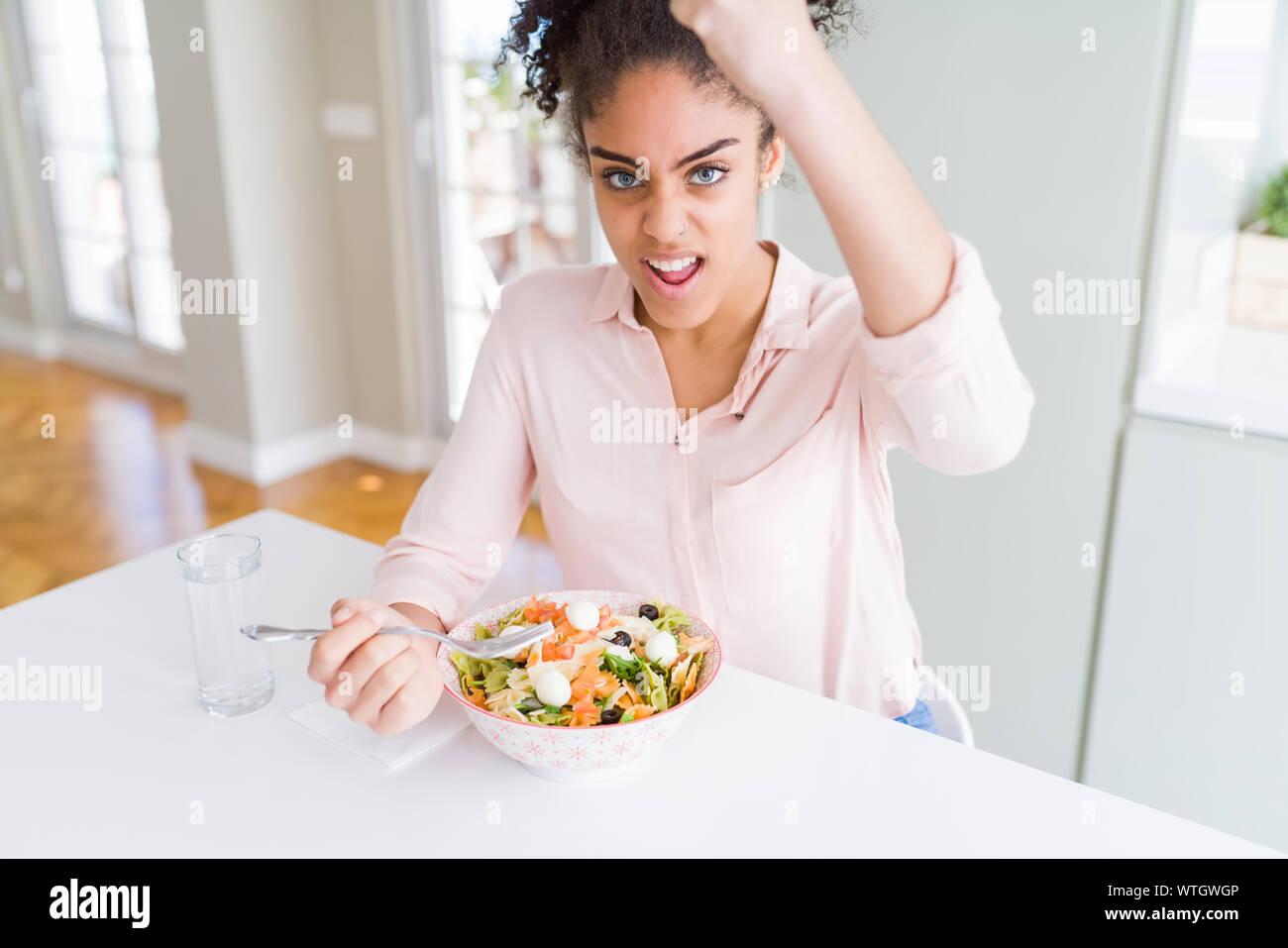 Young african american woman eating healthy pasta salad annoyed and ...
