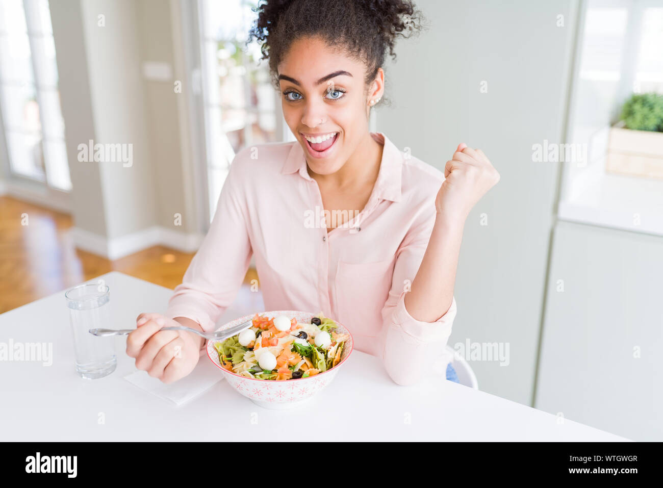 Young african american woman eating healthy pasta salad screaming proud ...