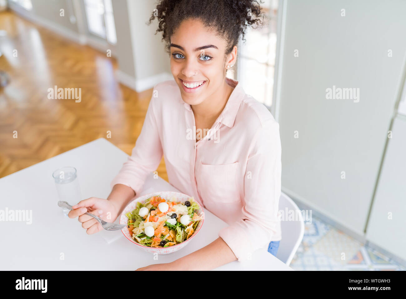 Young african american woman eating healthy pasta salad with a happy ...