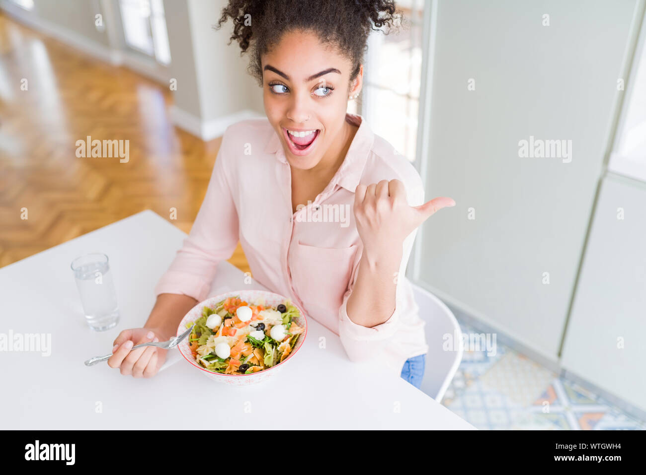Young african american woman eating healthy pasta salad pointing and ...