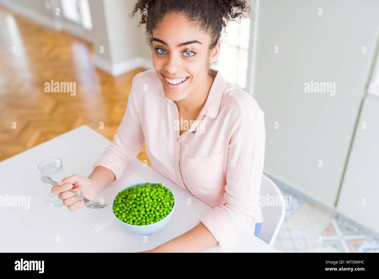 Young african american girl eating healthy green peas with a happy face standing and smiling ...