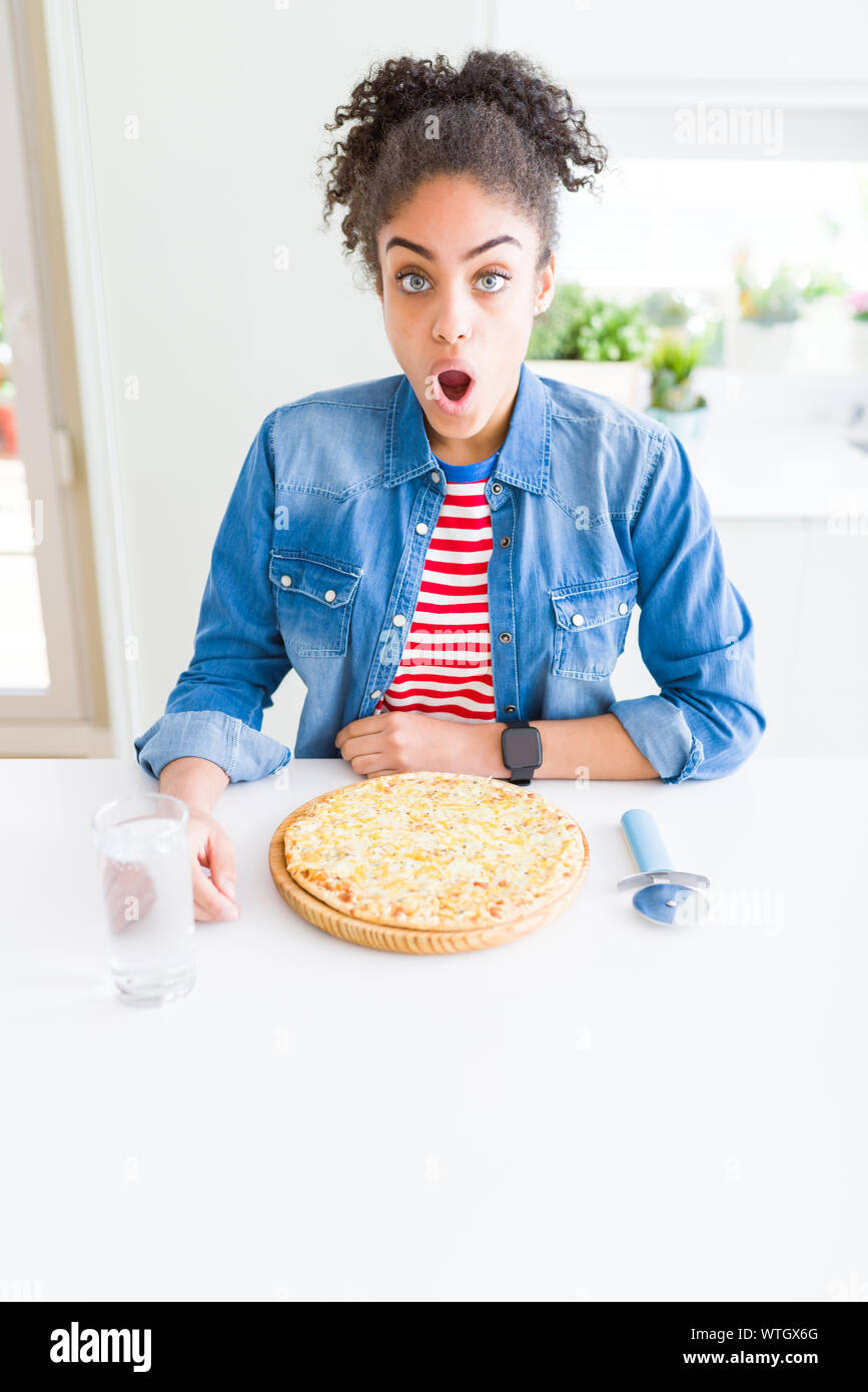 Young african american woman eating homemade cheese pizza scared in ...