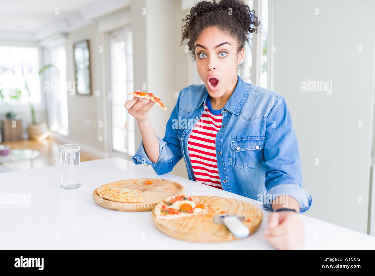 Young african american woman eating two homemade cheese pizzas scared ...