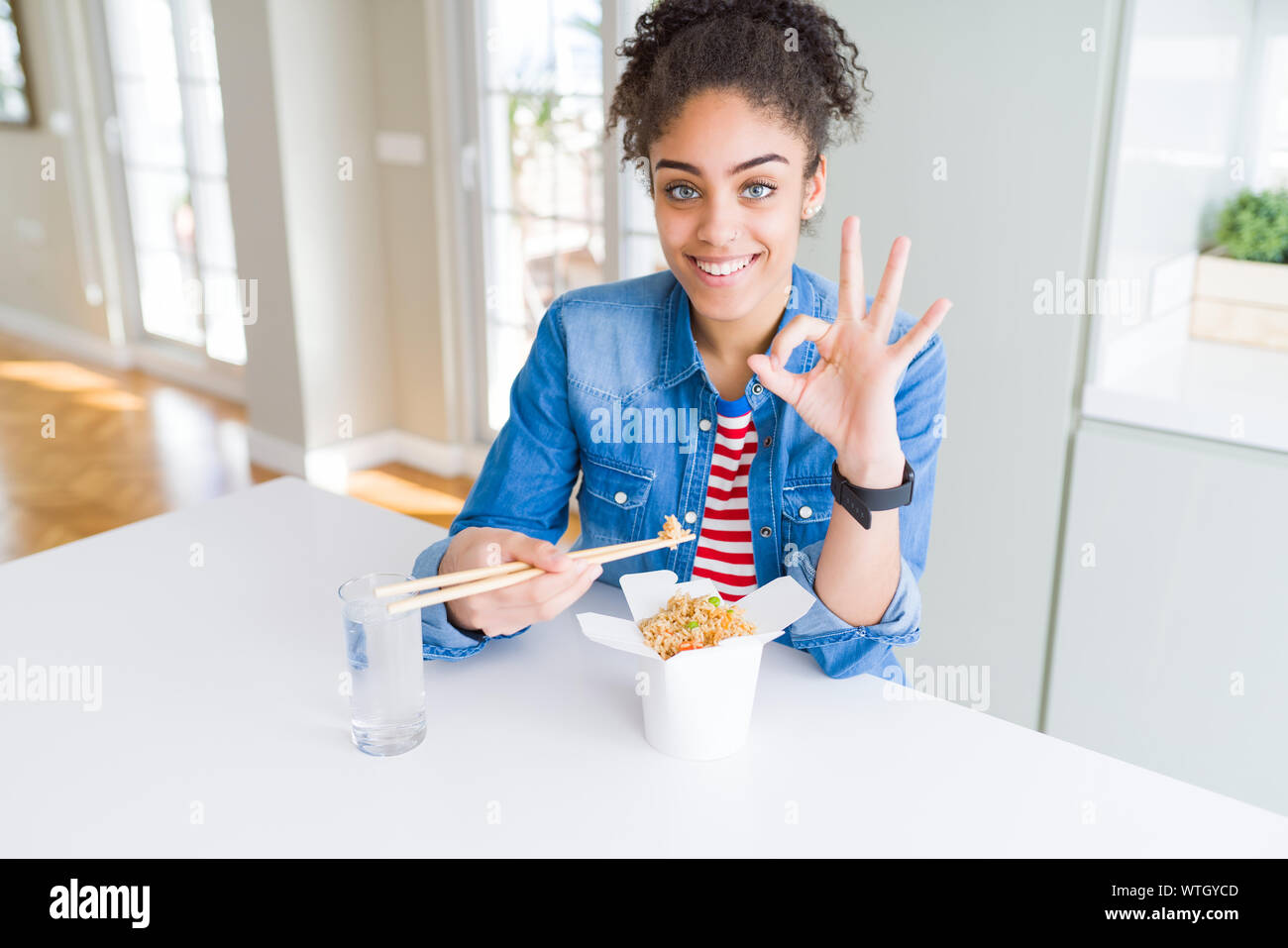 Young african american woman eating asian noodles from delivery box ...