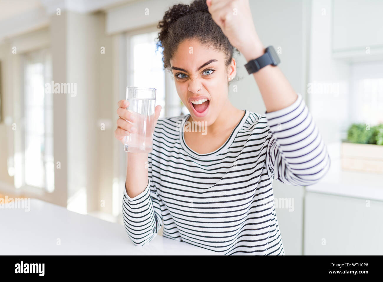 Young african american girl drinking a fresh glass of water annoyed and ...