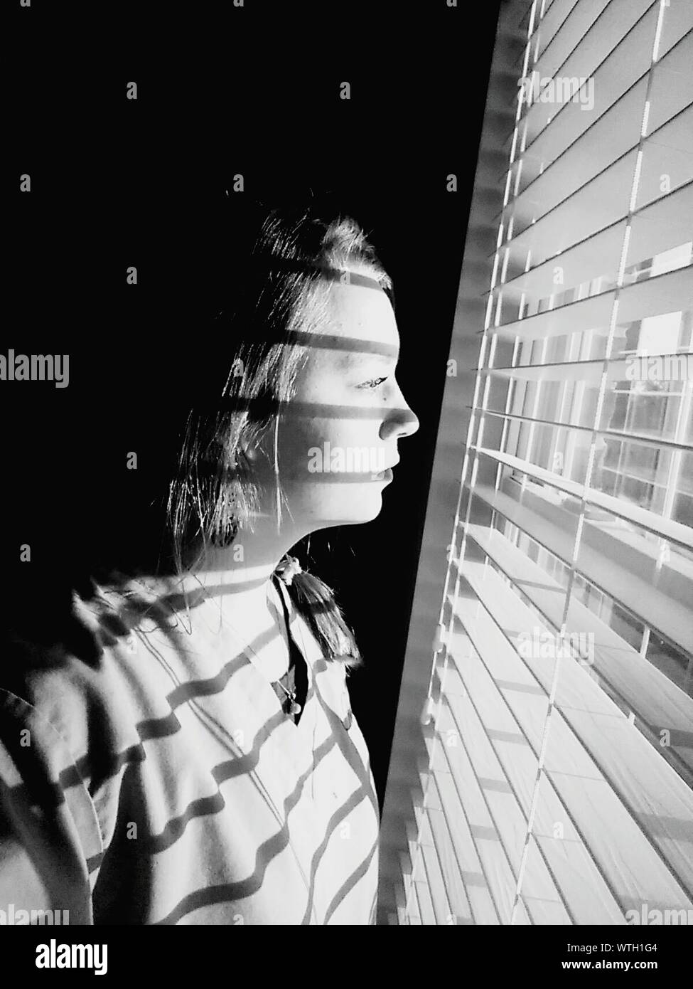 Woman in dark looking through blinds hi-res stock photography and ...
