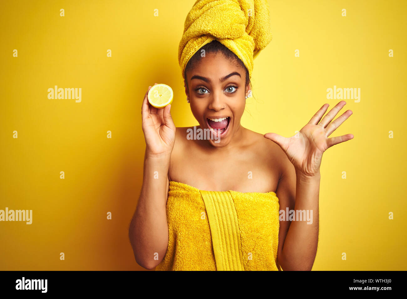 Afro woman wearing towel after shower holding slice lemon over isolated ...