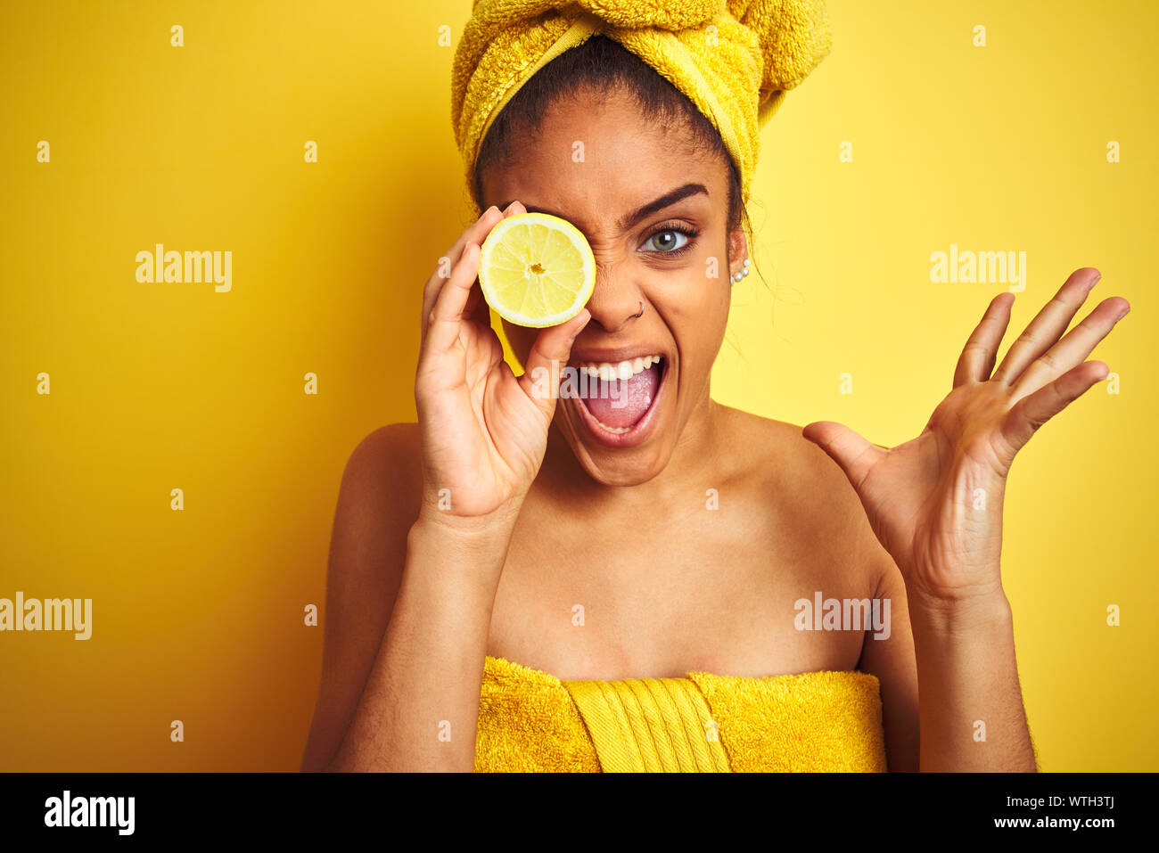 Afro woman wearing towel after shower holding slice lemon over isolated ...