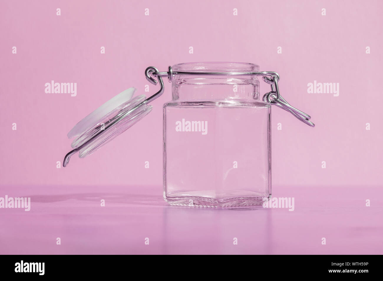 Empty glass jar with open lid and metal clasp on a pink background ...