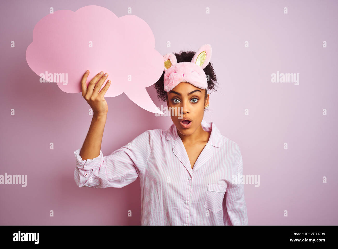 Afro woman wearing pajama and mask holding speech bubble over isolated ...