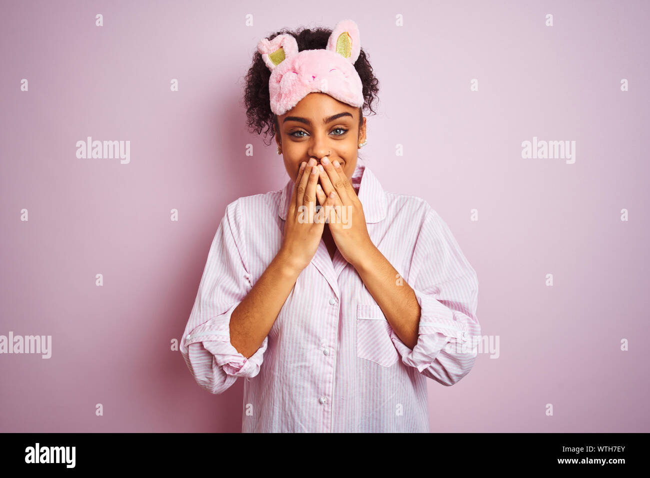 Young african american woman wearing pajama and mask over isolated pink ...