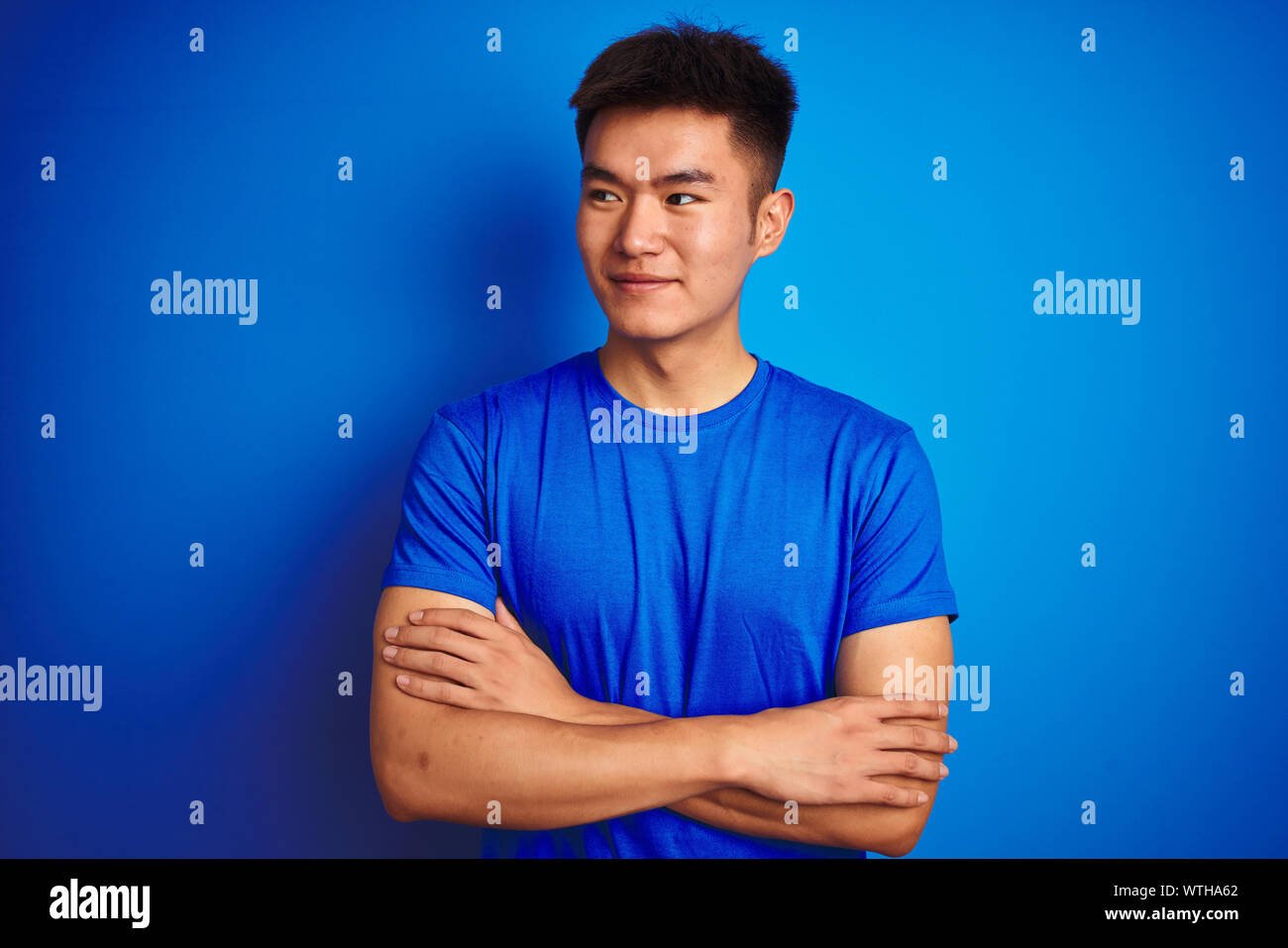Young asian chinese man wearing t-shirt standing over isolated blue ...