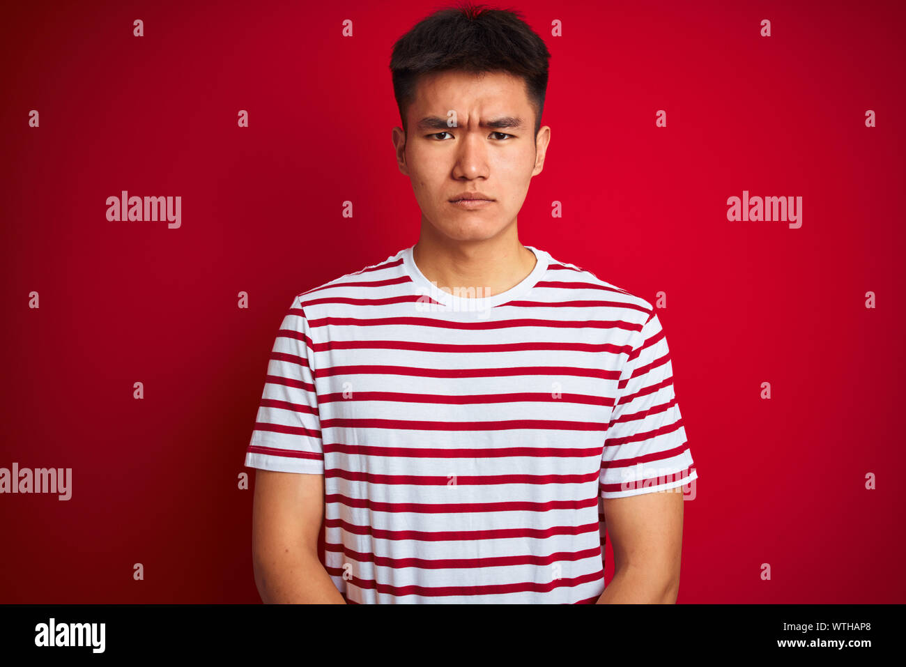 Young asian chinese man wearing striped t-shirt standing over isolated ...
