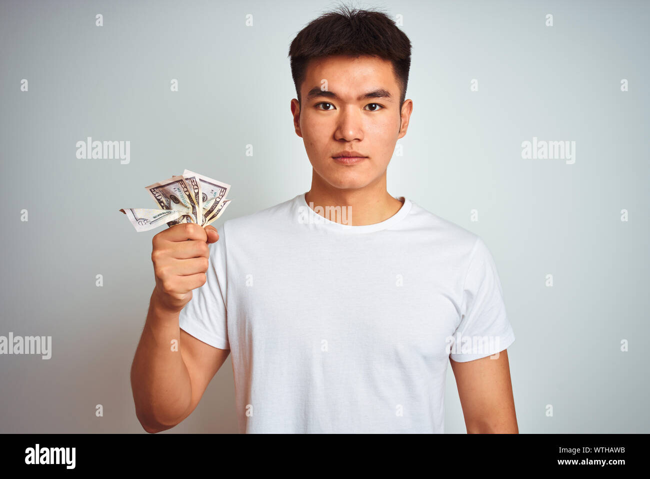 Young asian chinese man holding dollars standing over isolated white ...