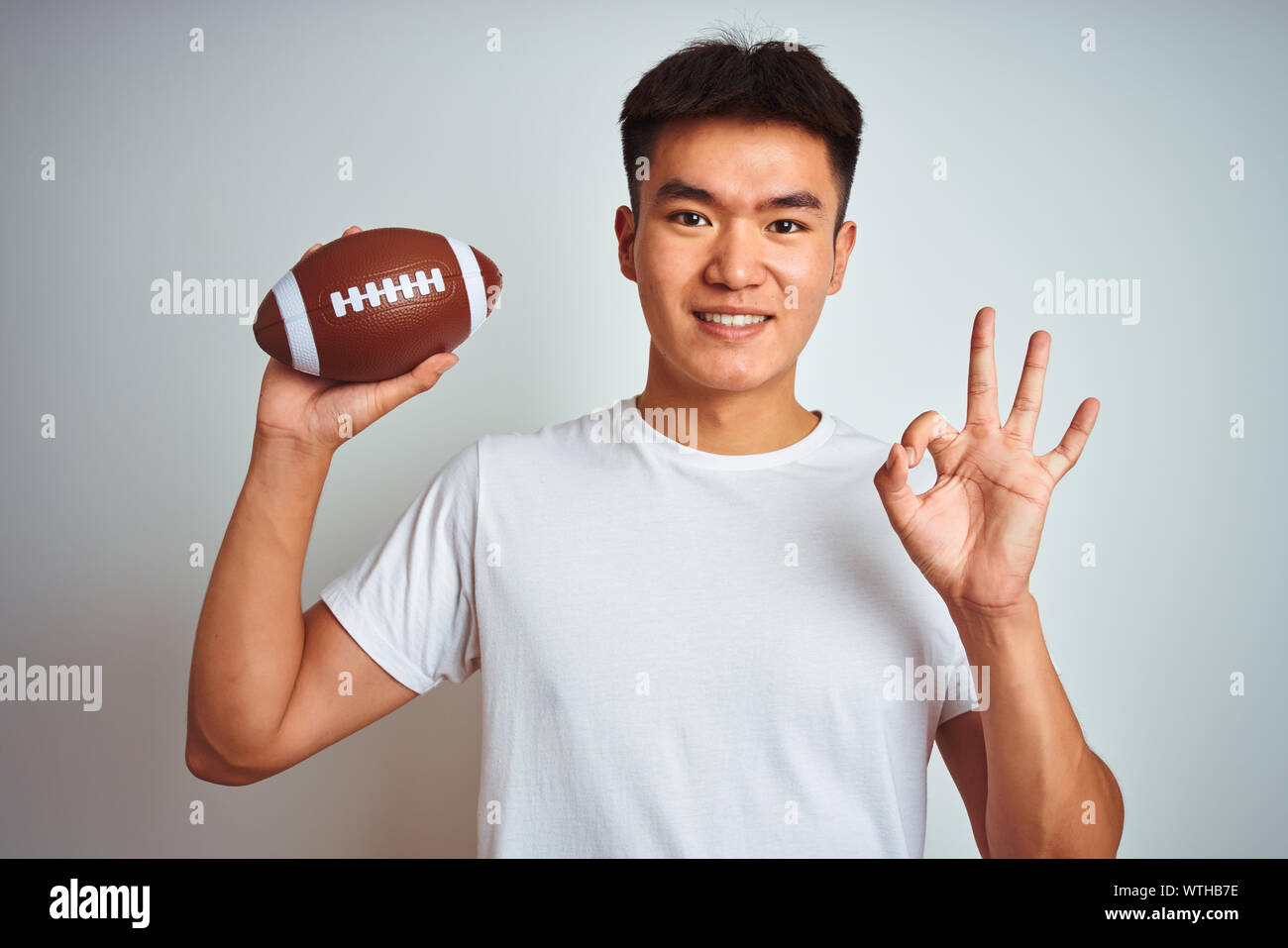 Young asian chinese sportsman holding rugby ball standing over isolated ...