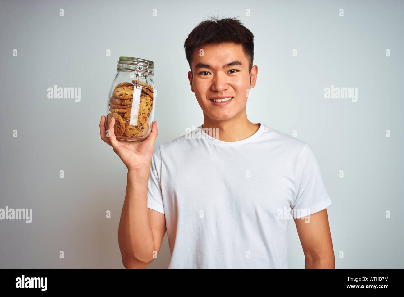 Young asian chinese man holding jar of cookies standing over isolated ...